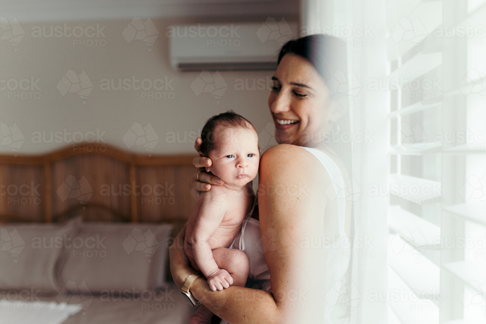 Image of Happy mother standing beside window holding newborn baby ...