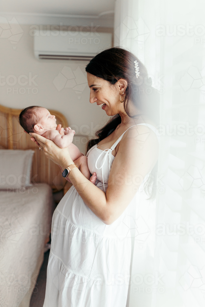 Image of Happy mother standing beside window holding newborn baby ...