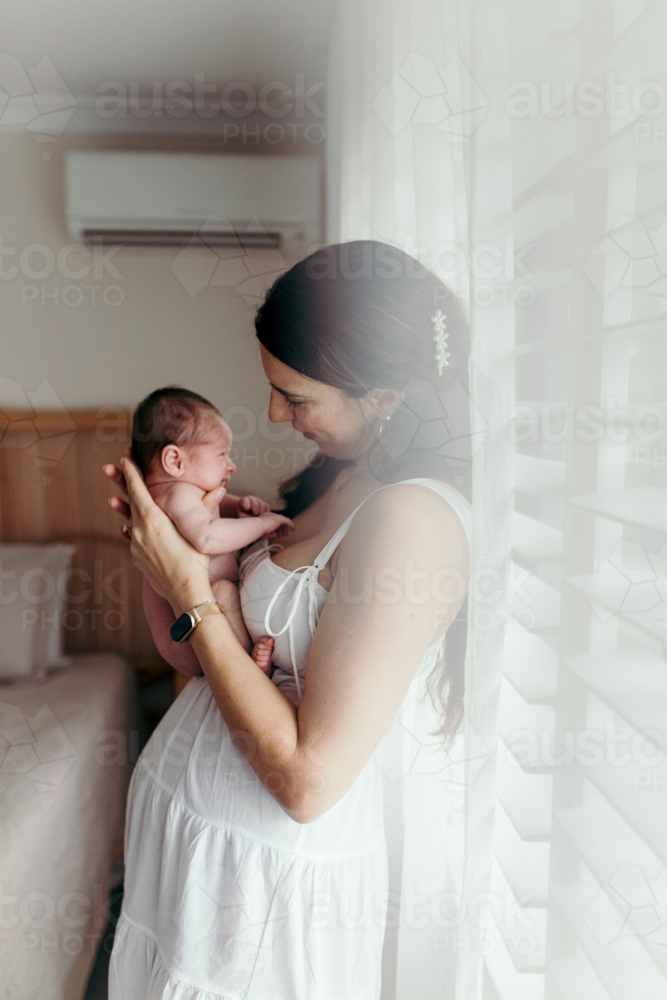Image of Happy mother standing beside window holding newborn baby ...