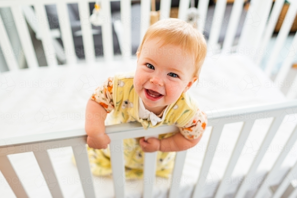 Image of Happy nine month old baby standing up in cot smiling in ...