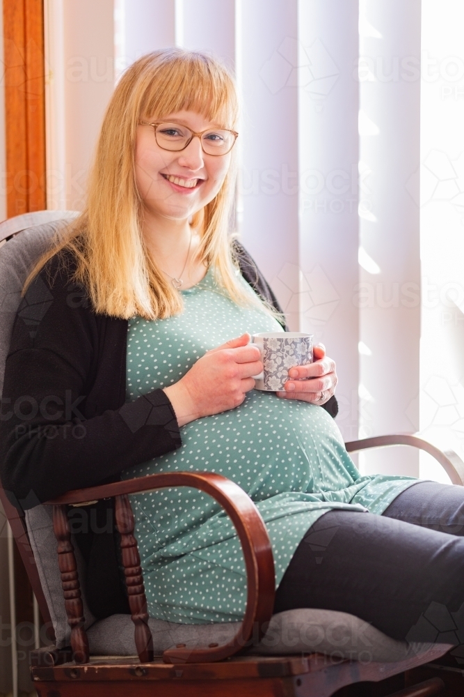 Image of Happy pregnant woman sitting in rocking chair with mug of ...