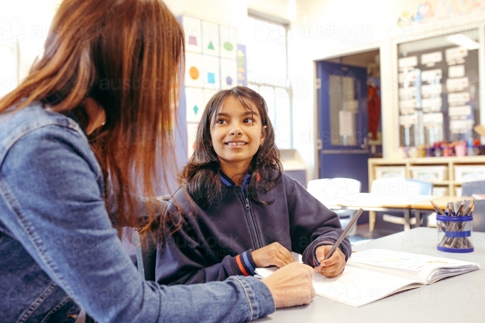 Image of Happy primary school student listening to her teacher whilst ...