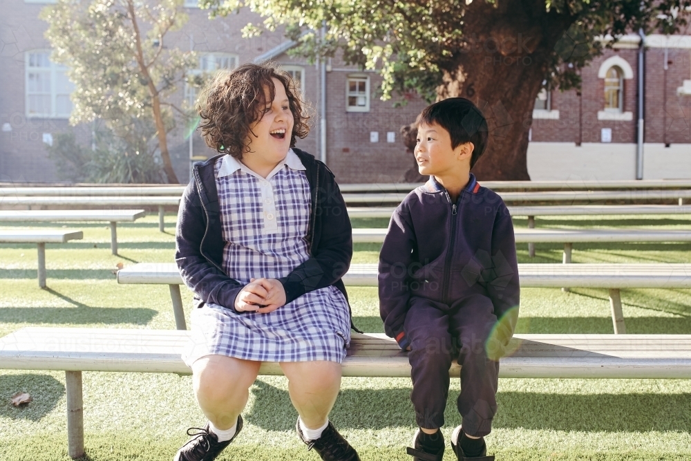 Image of Happy primary school students talking together on bench seats ...