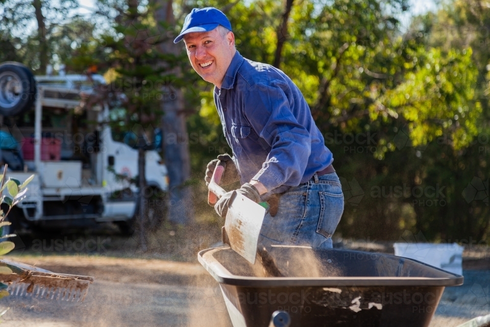 Image of Happy smiling man shoveling dry dusty dirt into a wheelbarrow ...
