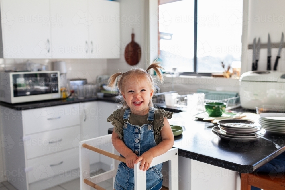 Image of Happy toddler girl standing in messy kitchen with dishes piled ...