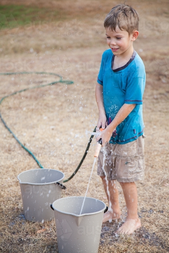 Image of Happy young boy rinsing out buckets for washing car - Austockphoto