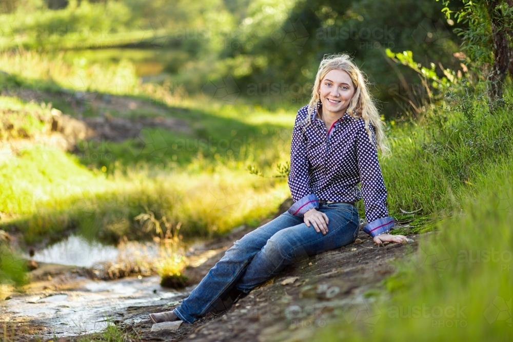 Image of Happy young country woman relaxing in shade by the creek ...