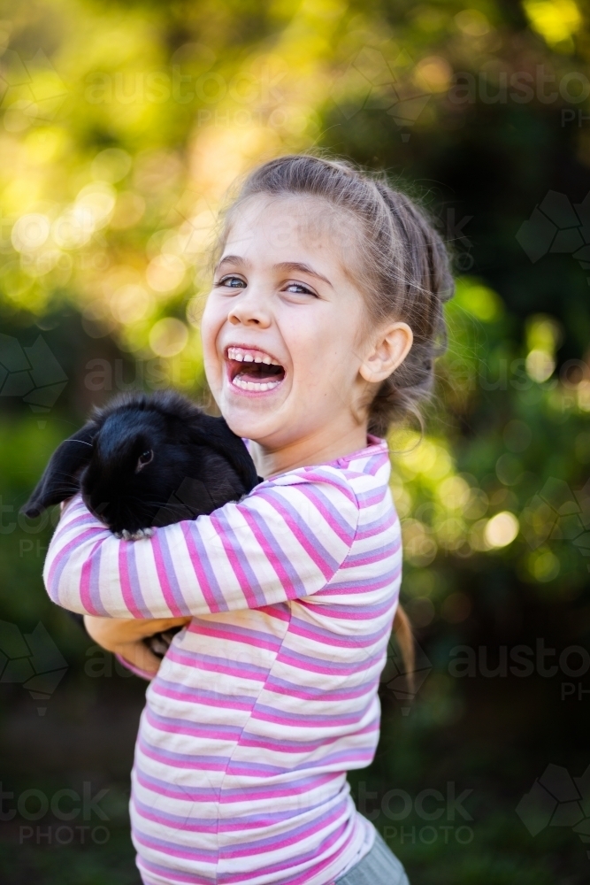 Image of Happy young kid laughing and cuddling black pet bunny rabbit ...