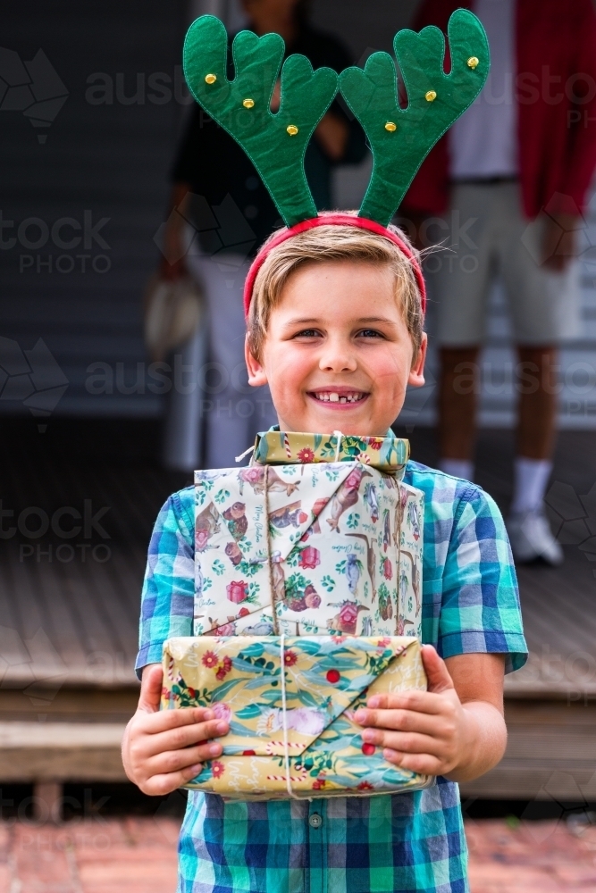 Image of Happy young kid with pile of Christmas gifts and silly antlers ...