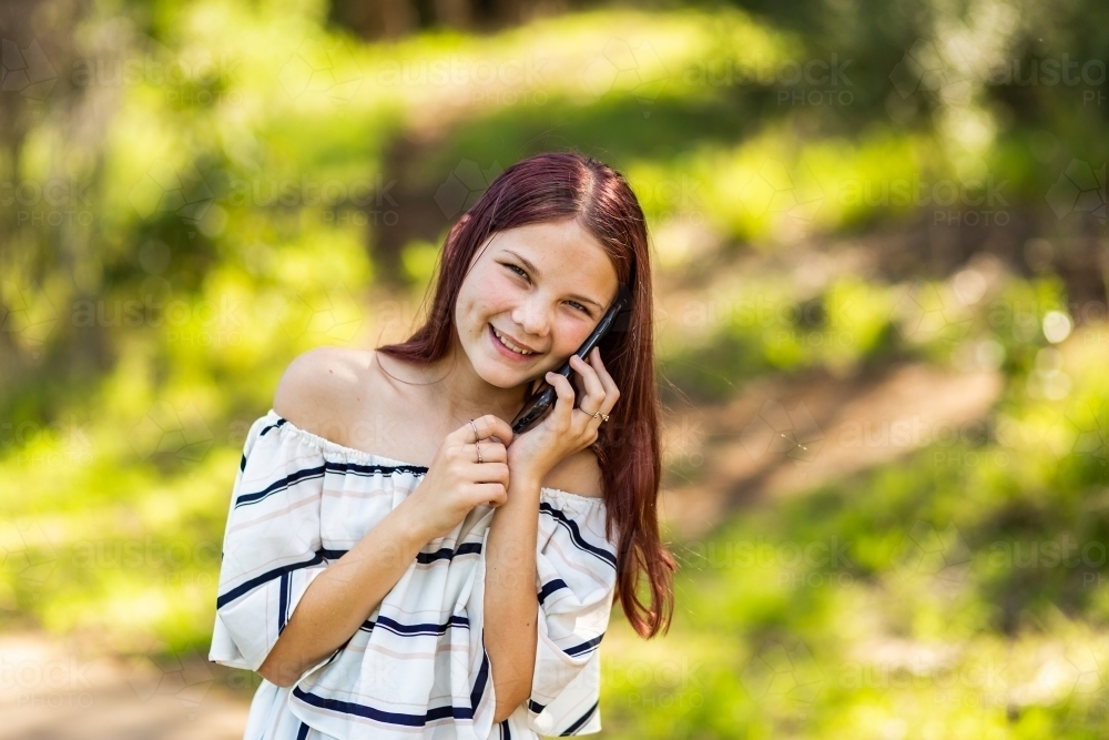 Image of Happy young tween girl on phone outdoors in parkland ...