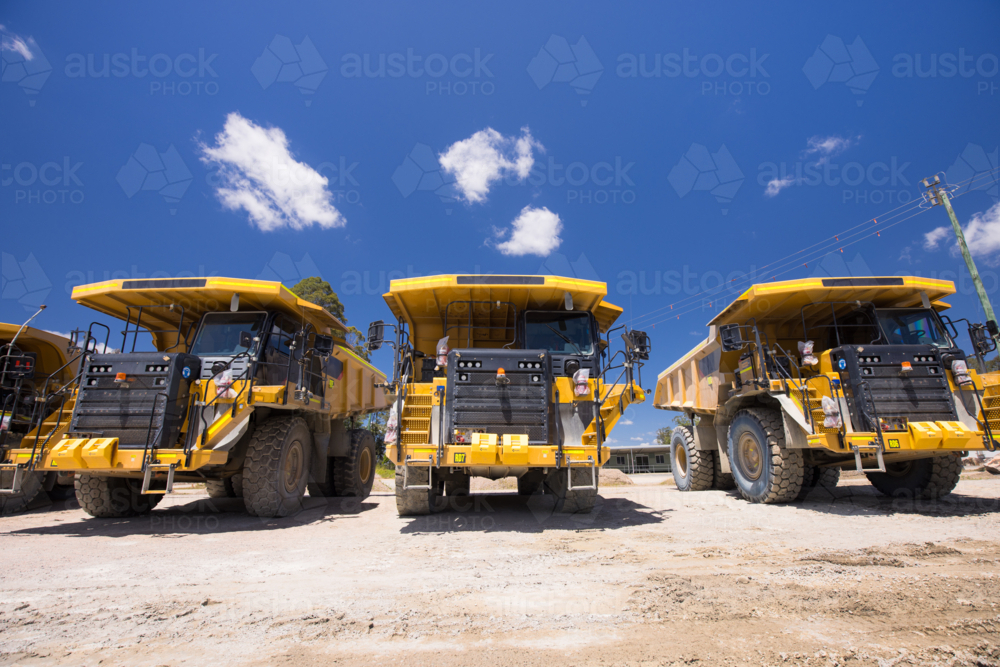 Image of Haul trucks lined up in a quarry worksite on a sunny day ...