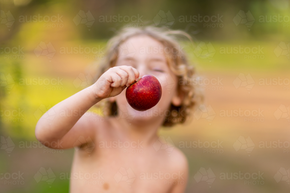 Image of head and shoulders of young child holding red apple up in ...