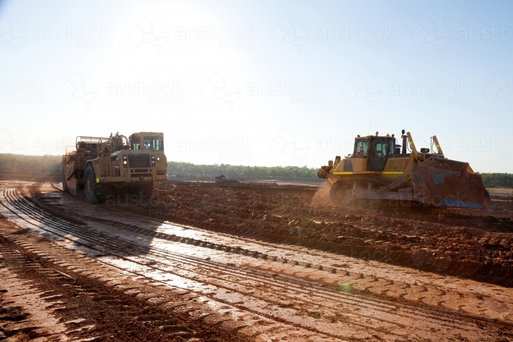 Image of Heavy machinery flattening dirt to build a road - Austockphoto