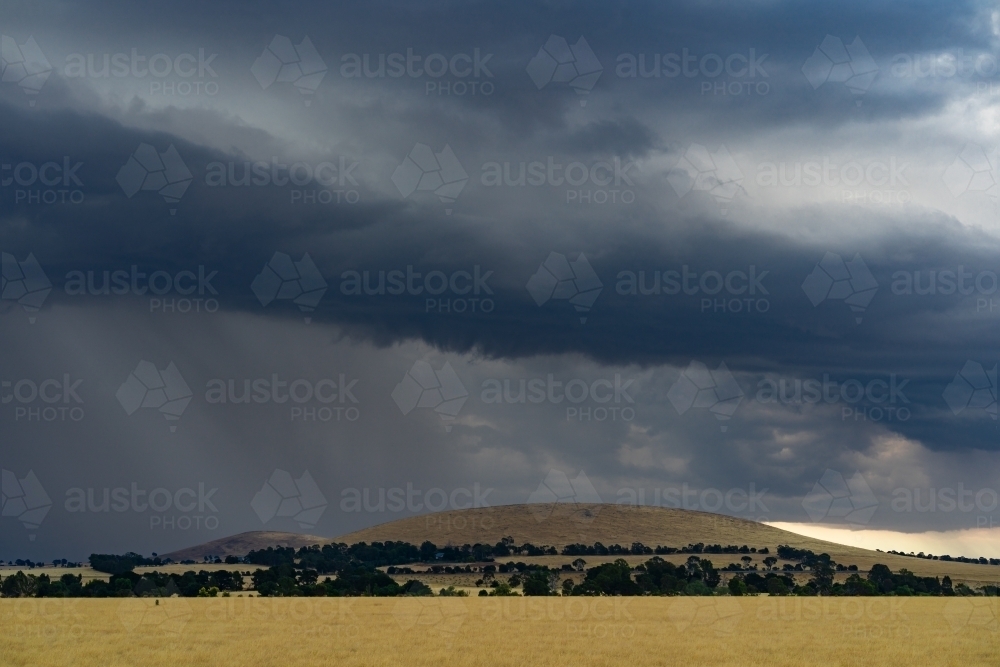 Image of Heavy rain and a dark shelf cloud over a dry barren hill on ...