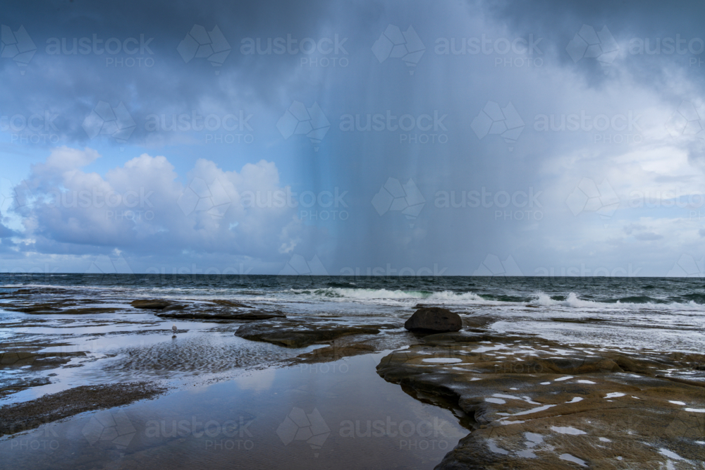 Image of Heavy rain storm falling over coastal rockpools at Kings Beach ...
