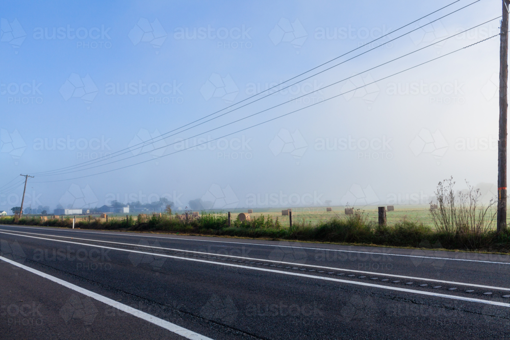 Image of highway with powerline on roadside and paddock of haybales ...
