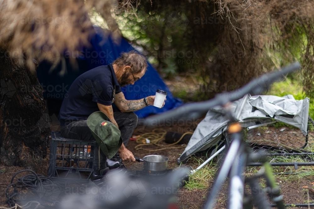 Image of Homeless man pouring water from his camp stove into a cup ...