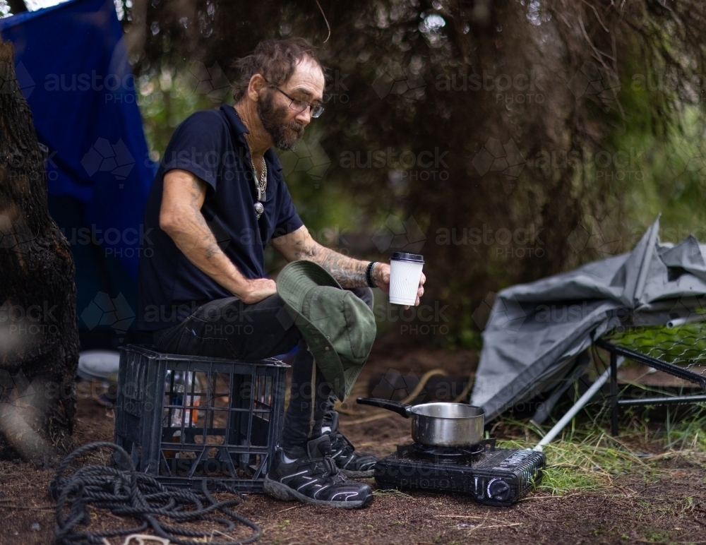 Image of homeless man sitting on milk crate near butane stove in front ...