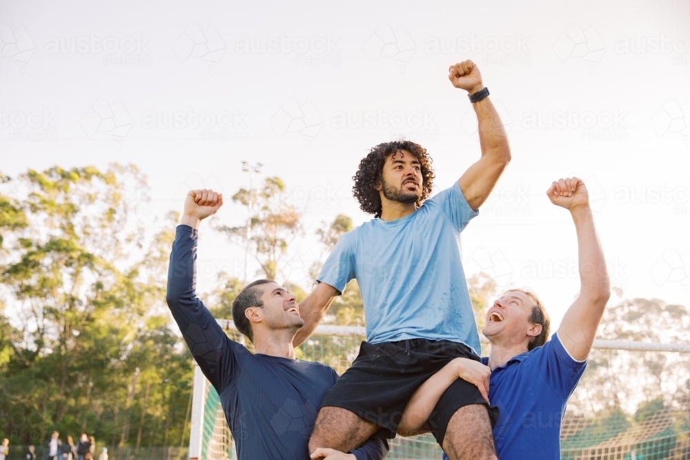 Image of horizontal shot of two men carrying a man on their shoulders ...