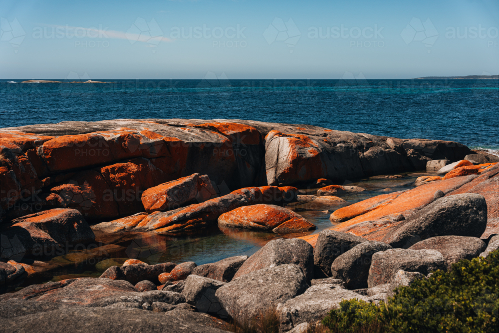 Image of Huge reddish rocks along the shoreline with blue waters ...