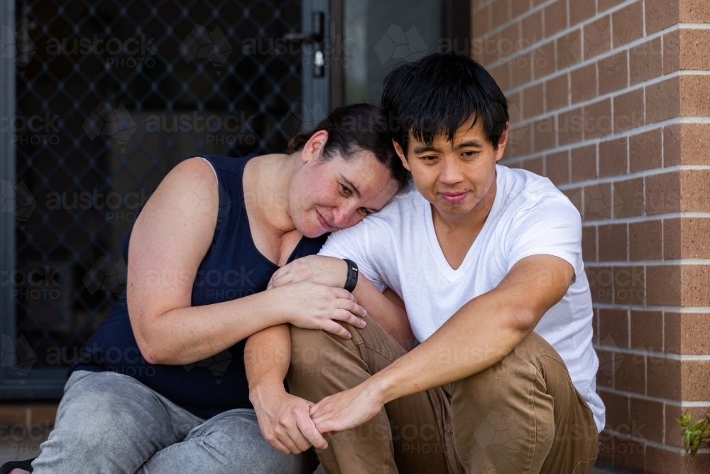 Image of husband and wife sitting on front steps of house hugging each ...