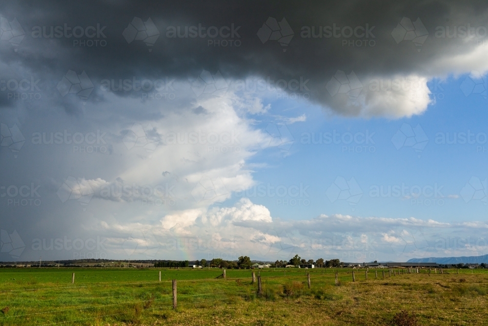 Image of Incoming storm with distant rain on farmland and rainbow in ...