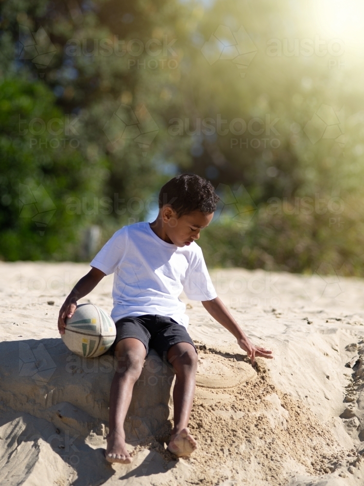 Image of Indigenous boy playing with ball on a sand ledge at beach ...