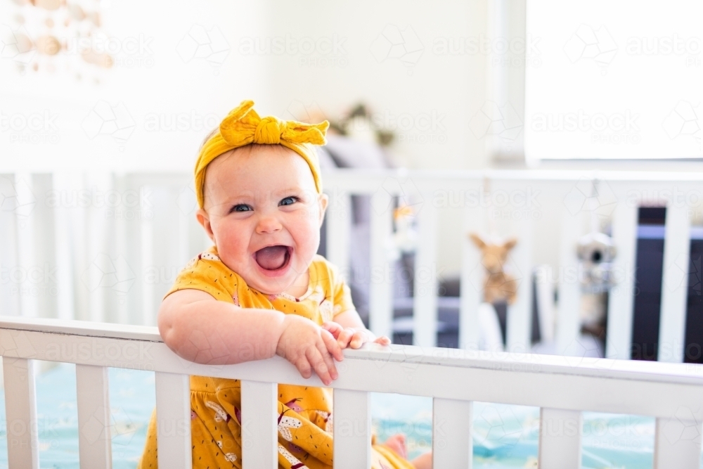 Image of Joyful happy baby sitting in cot in bedroom with copy space ...