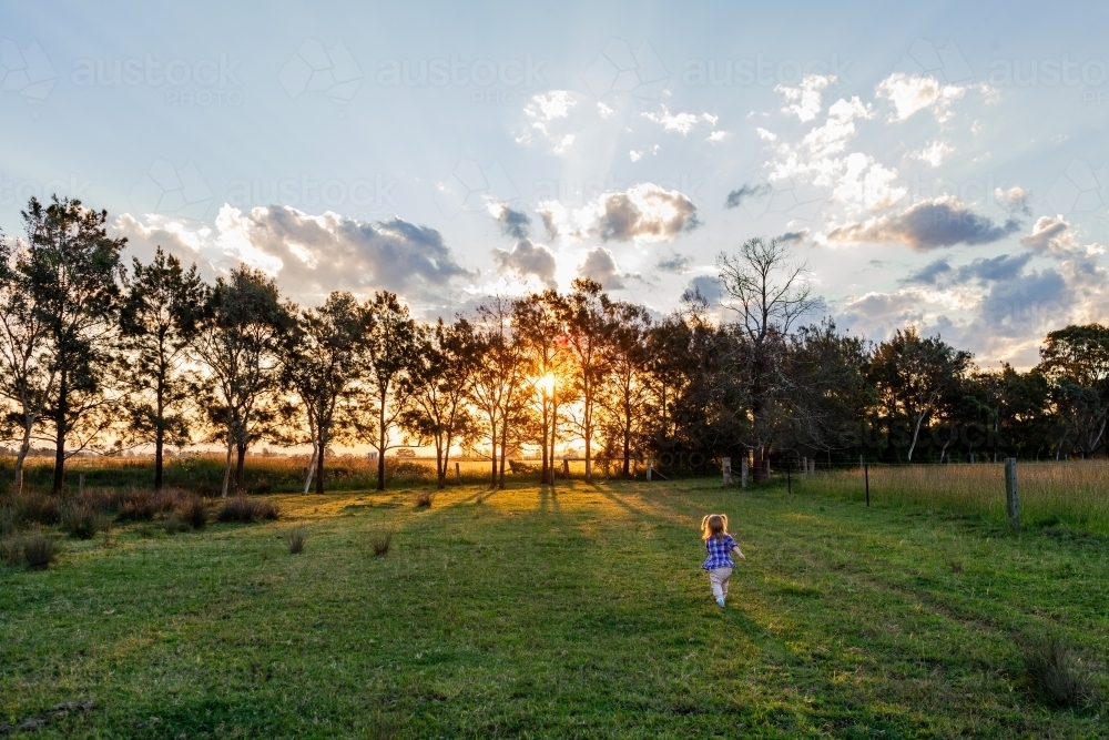 Image of Kid running towards trees along farm fence line at sunset at ...