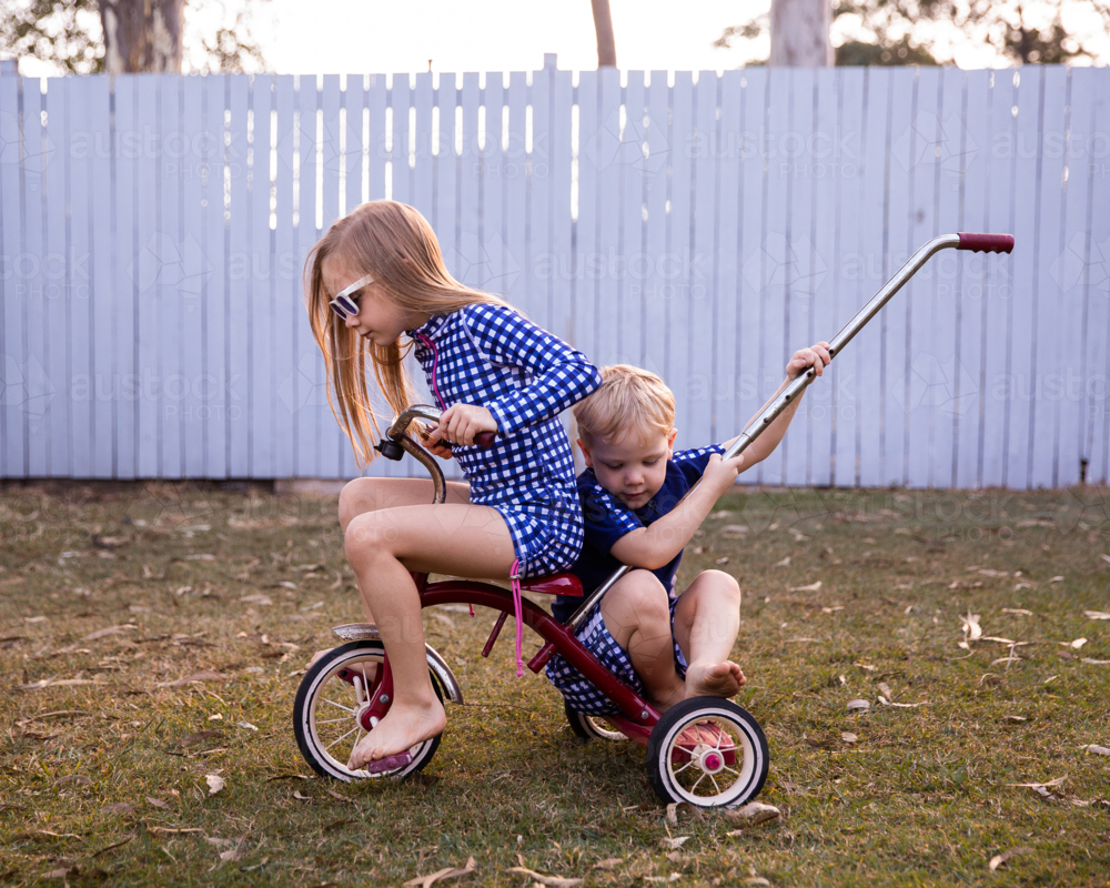 Image of kids playing on a trike in their back yard - Austockphoto