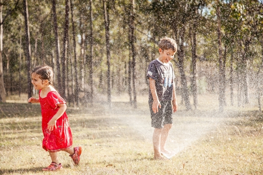 Image of Kids playing under a sprinkler in summer - Austockphoto