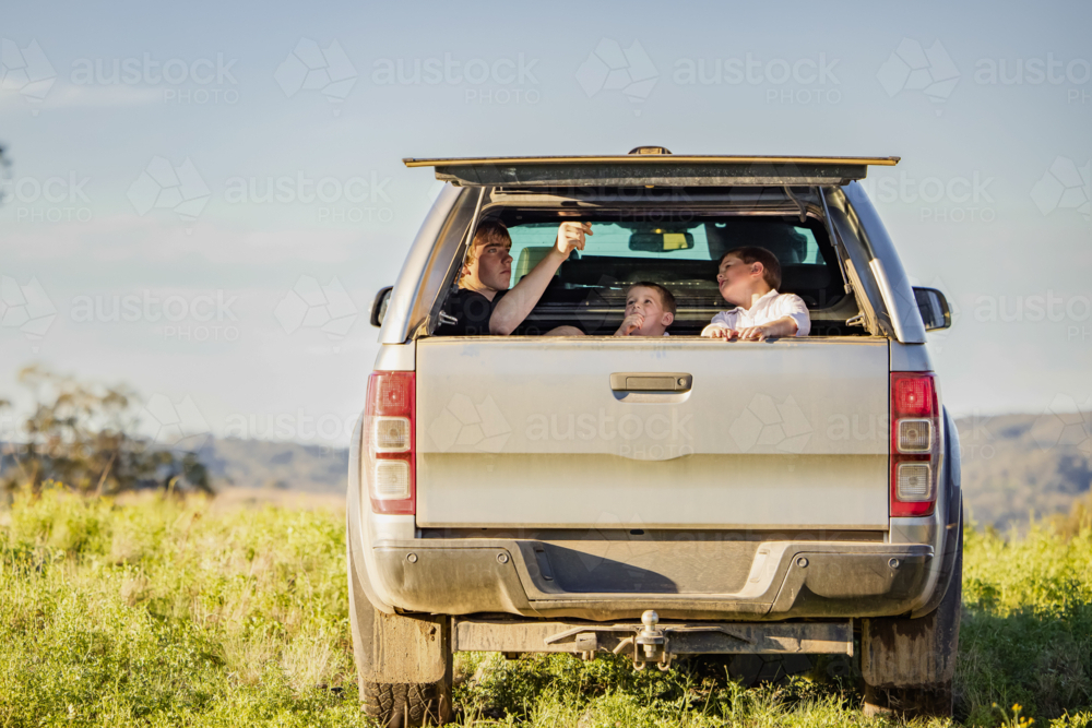Image of Kids sitting in the back of ute on farm - Austockphoto