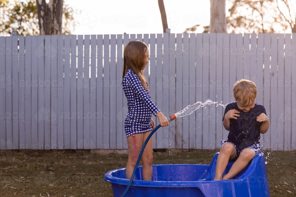 Image of kids splashing each other with the hose in a paddle pool ...