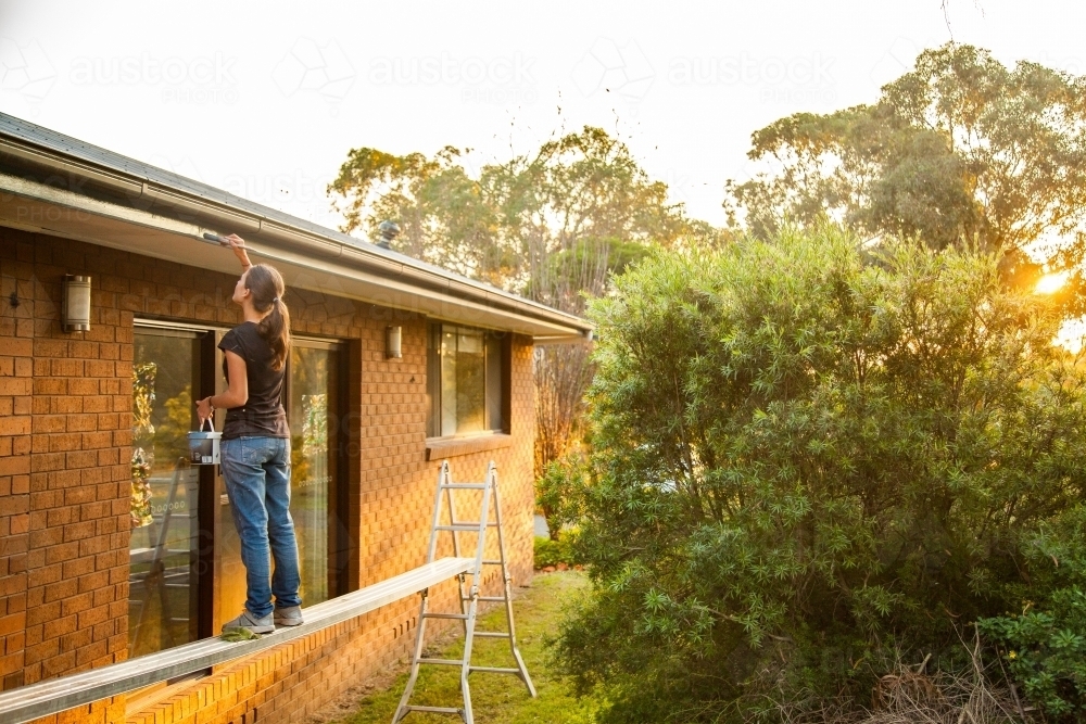 Image of Lady tradie painting house bargeboards in afternoon light ...