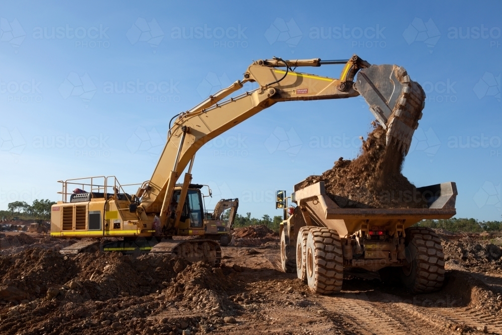 Image of Large digger moving dirt into an earth mover on an industrial ...