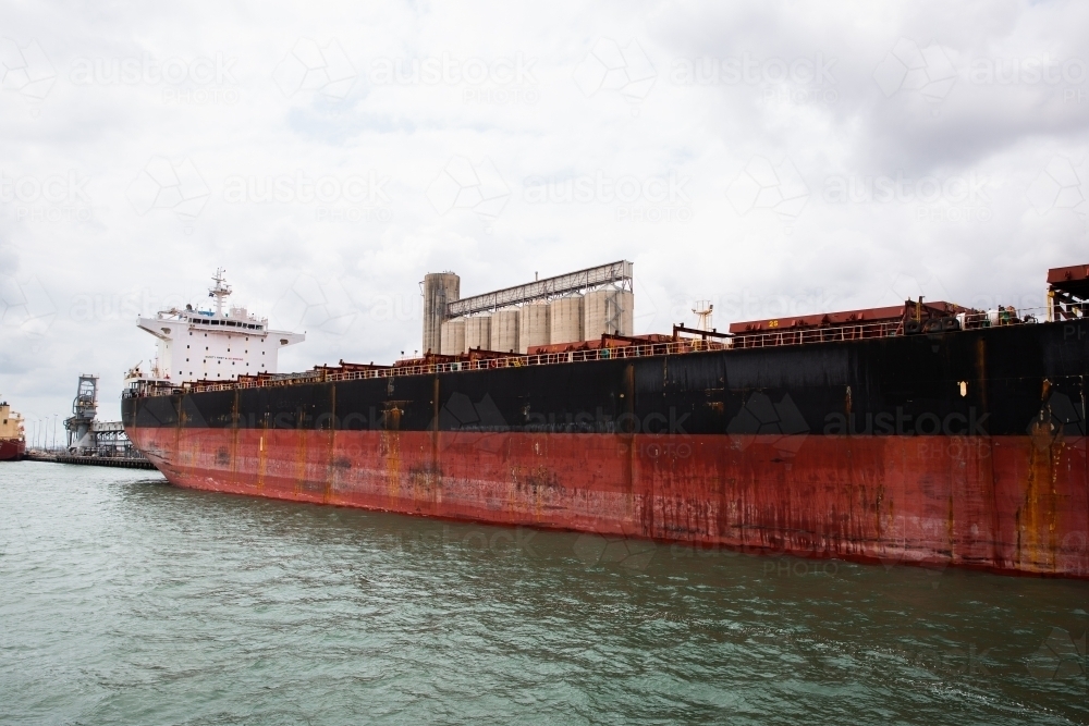 Image of large red and black ship docked next to silos in Gladstone ...