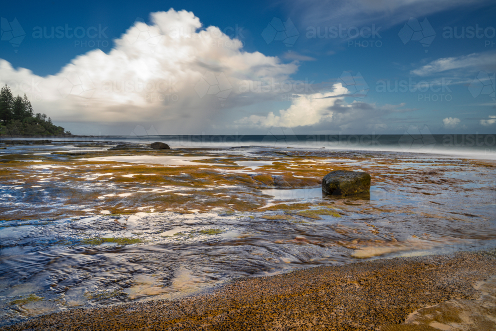 Image of Large storm cloud reflected in water running over a coastal ...