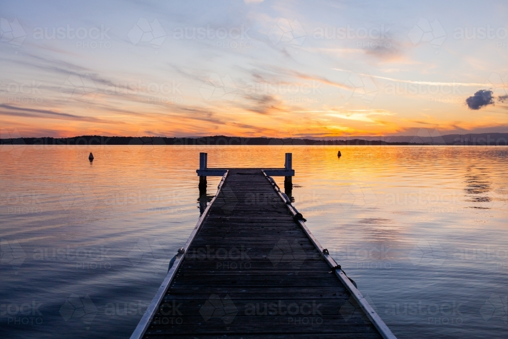 Image of Leading lines of jetty out in coastal lake waters at sunset ...