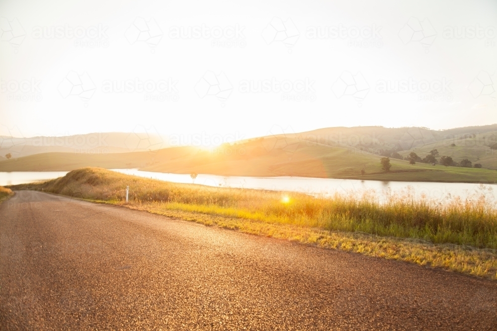 Image of Lens flare and sunlight shining over lake beside road ...