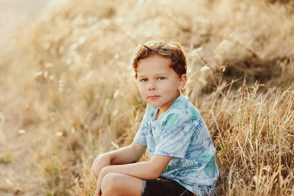 Image of Little aboriginal Australian boy sitting in long dry grass ...