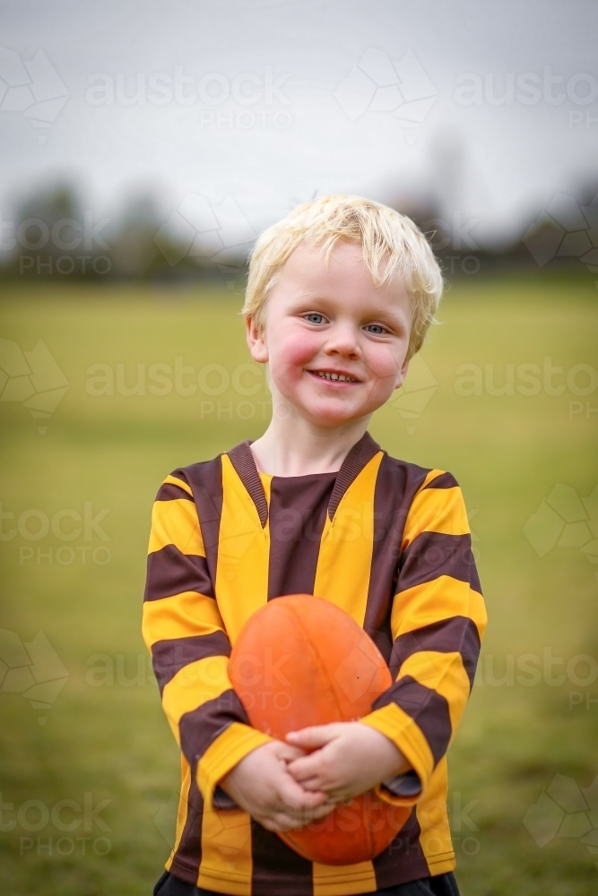 Image of Little boy in Aussie Rules Football uniform on field with ball ...