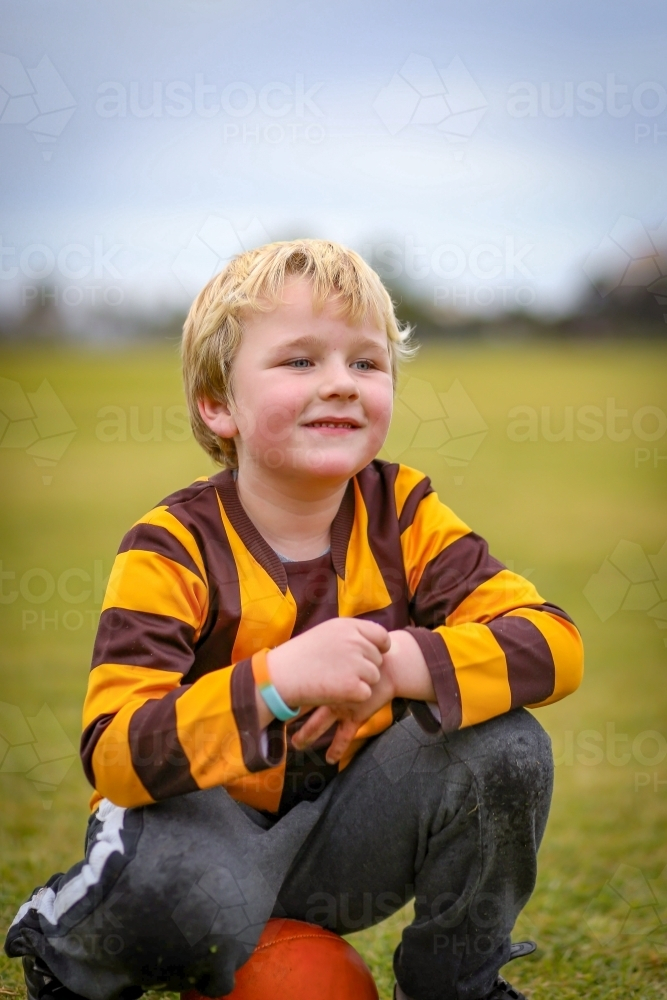 Image of Little boy in Aussie Rules Football uniform on field with ball ...