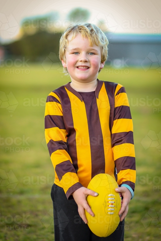 Image of Little boy in Aussie Rules Football uniform on field with ball ...