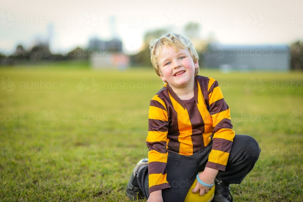 Image of Little boy in Aussie Rules Football uniform on field with ball ...