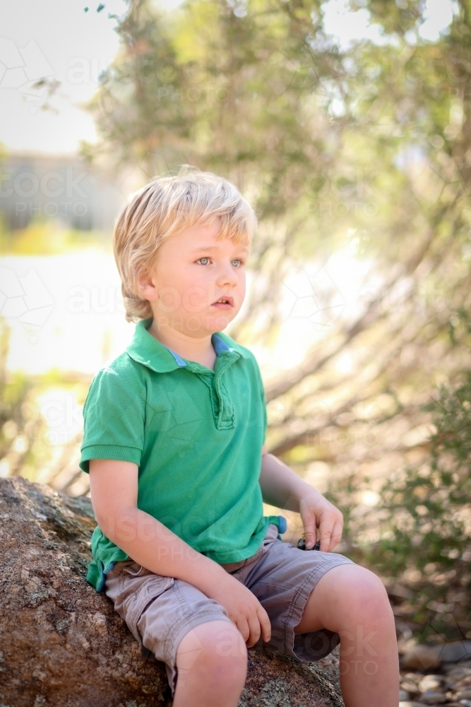 Image of Little boy sitting in kindergarten yard with serious ...