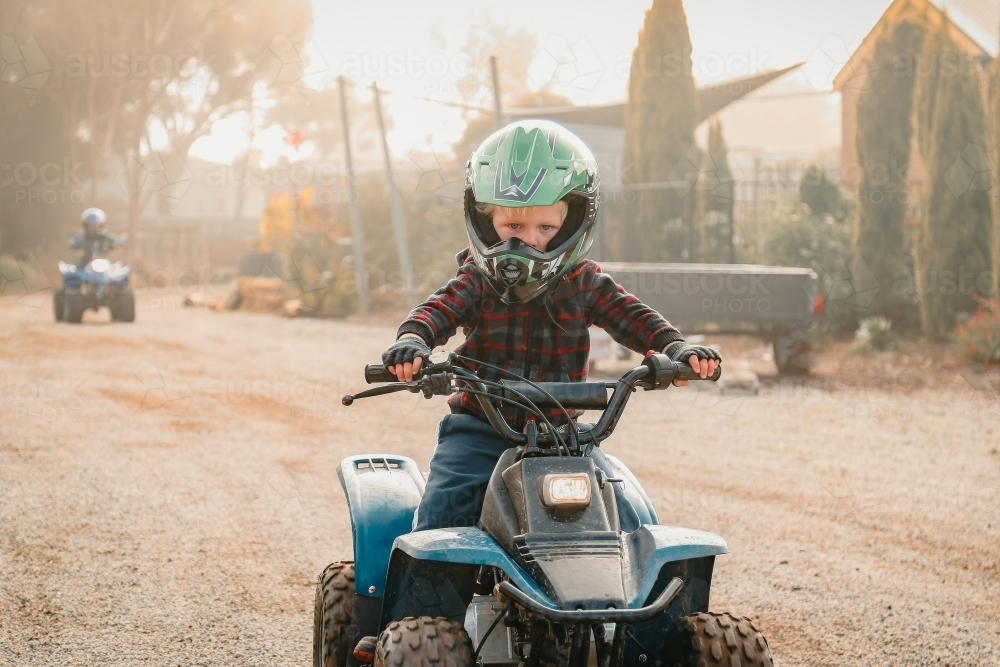 Image of Little boys riding quad bikes on farm - Austockphoto