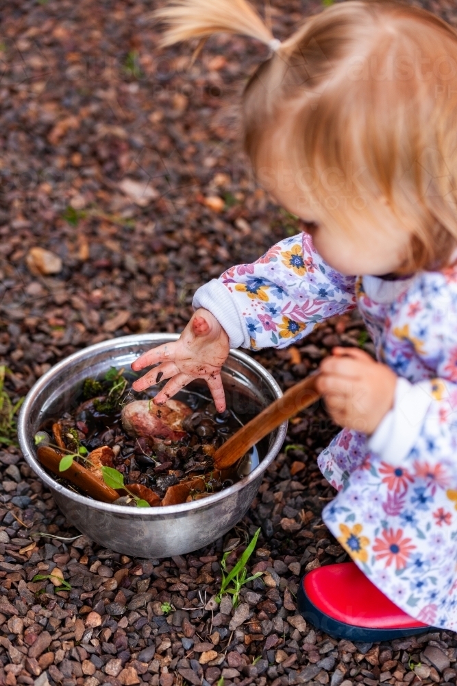 Image of Little girl in imaginative play making a stew of rocks in bowl ...