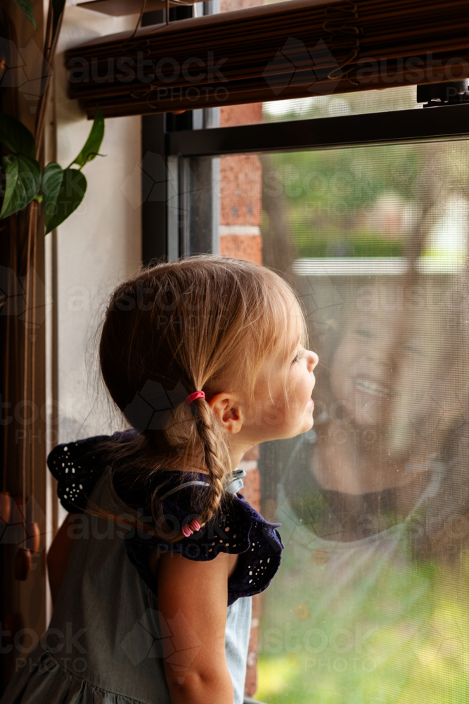 Image of Little girl indoors looking out front window of home ...