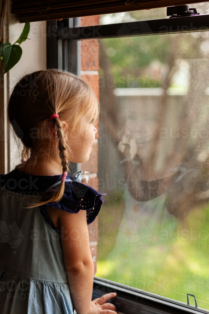 Image of Little girl indoors looking out front window of home ...