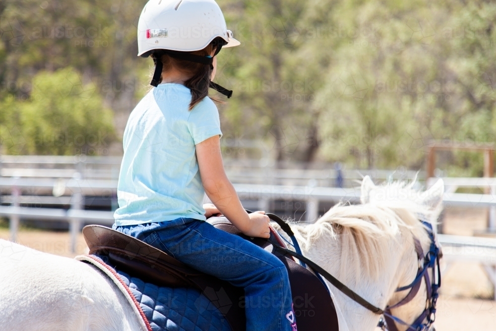 Image of Little girl riding a white pony in dusty yard at riding school ...